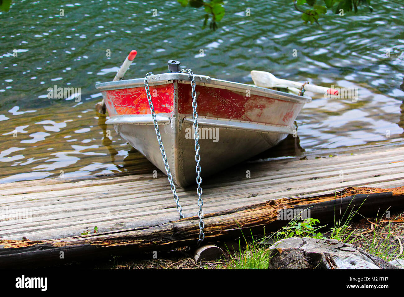 An aluminum row boat chained to the shore by a dock Stock Photo - Alamy