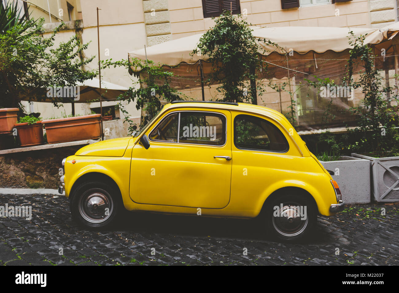 A yellow small car in a roman street with stones and plants in the ...