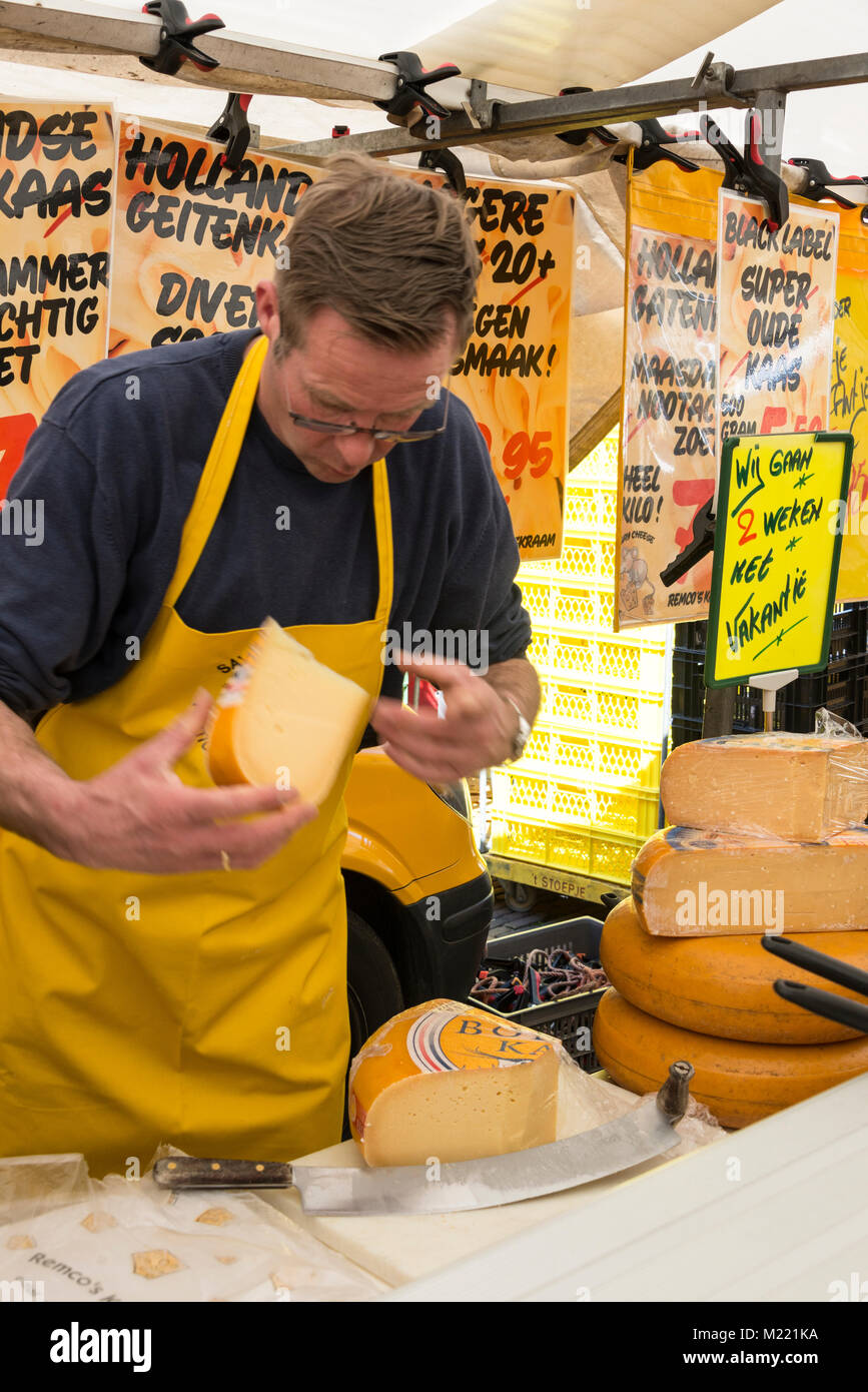 A Dutch cheese seller cutting a piece of cheese for a customer at one ...