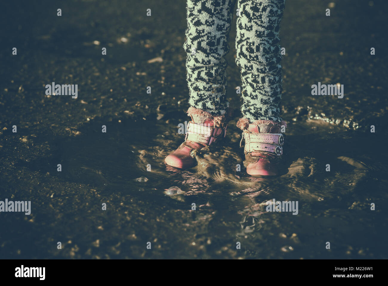 Little girl is playing in water, wet dirty shoes, in the middle of ...