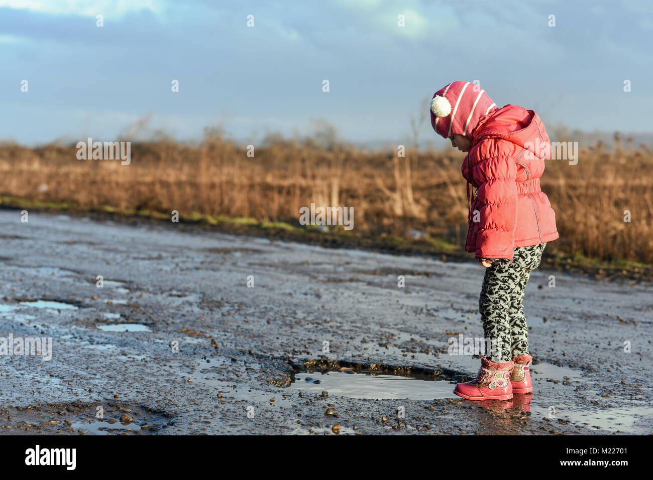 Concept - happy childhood. Little girl looking into the puddle ...
