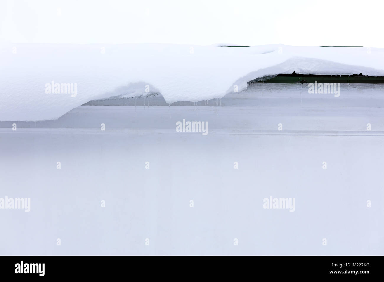 melting snow overhanging on the roof down to white building wall Stock ...