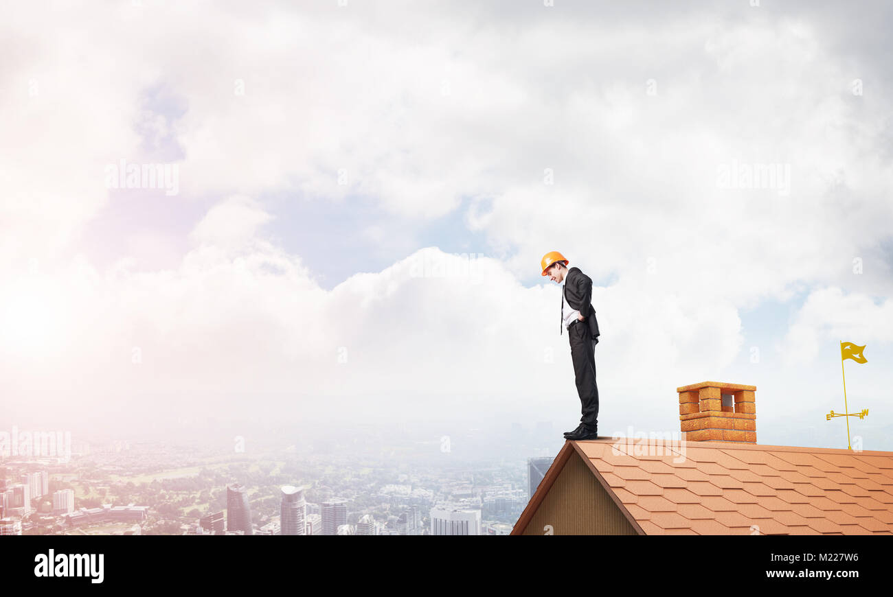Businessman looking down from roof and modern cityscape at background ...