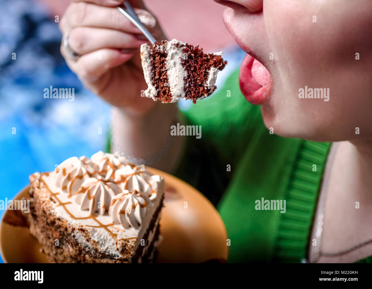 The woman opens her mouth to eat a piece of cake. In her hand she holds ...