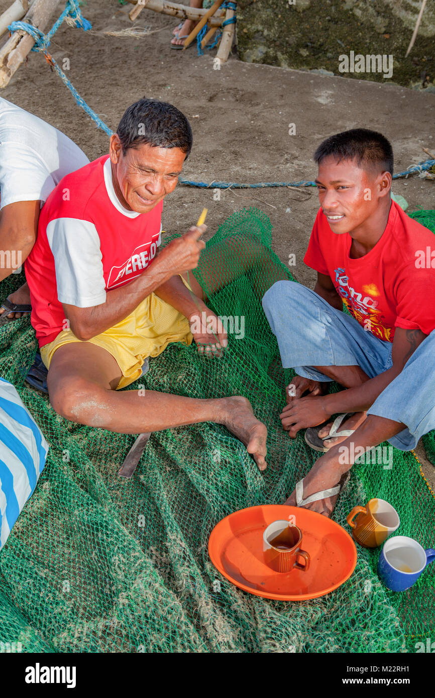 Weathered Filipino fishermen relax over coffee while mending their ...