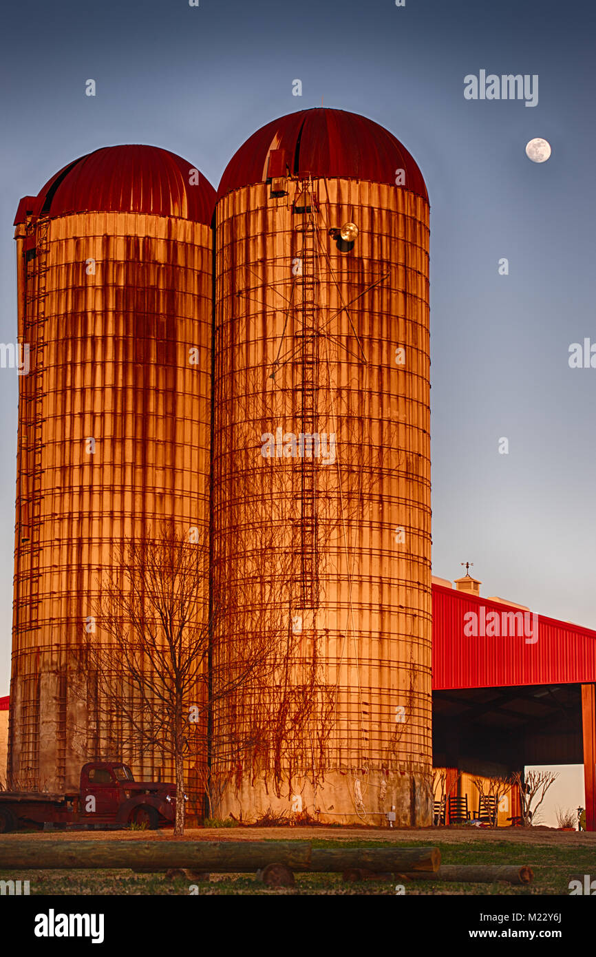 Vertial photo of two silos colored by the sunset with an old vehicle ...