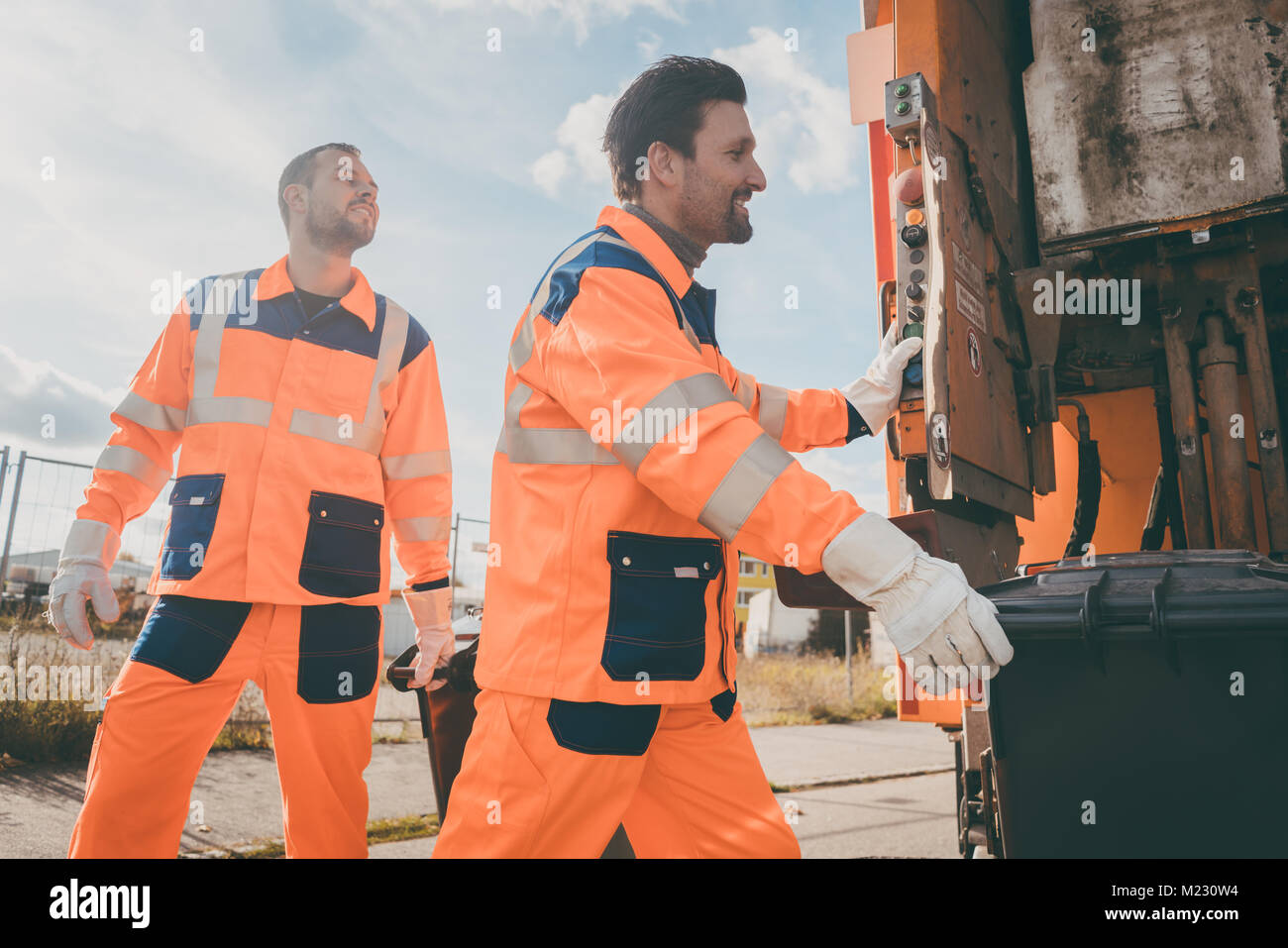 Two garbagemen working together on emptying dustbins Stock Photo - Alamy