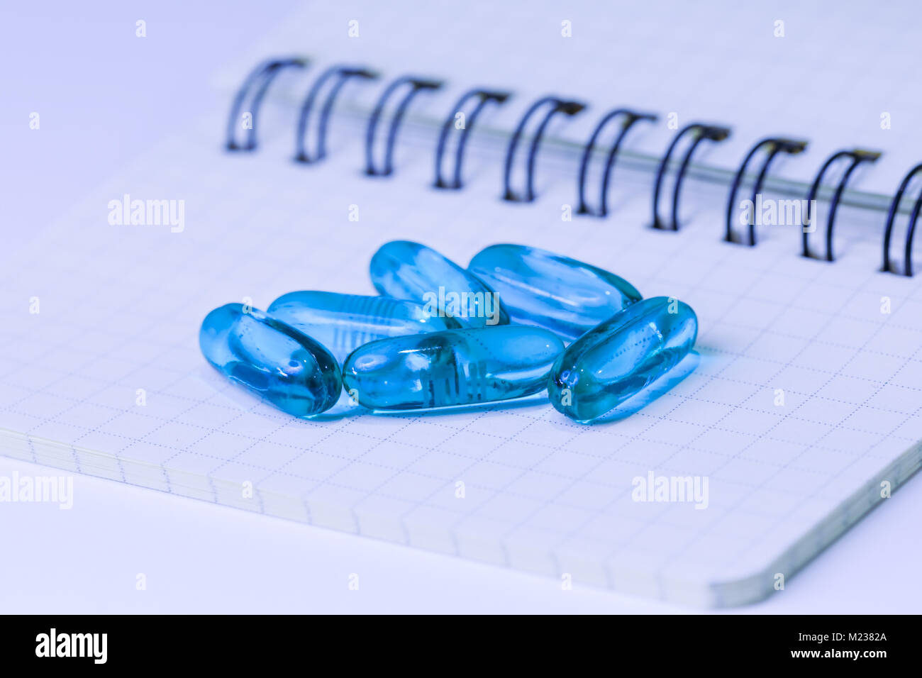 Blue pills in capsule shape scattered on a white sheet. Blue pills ...