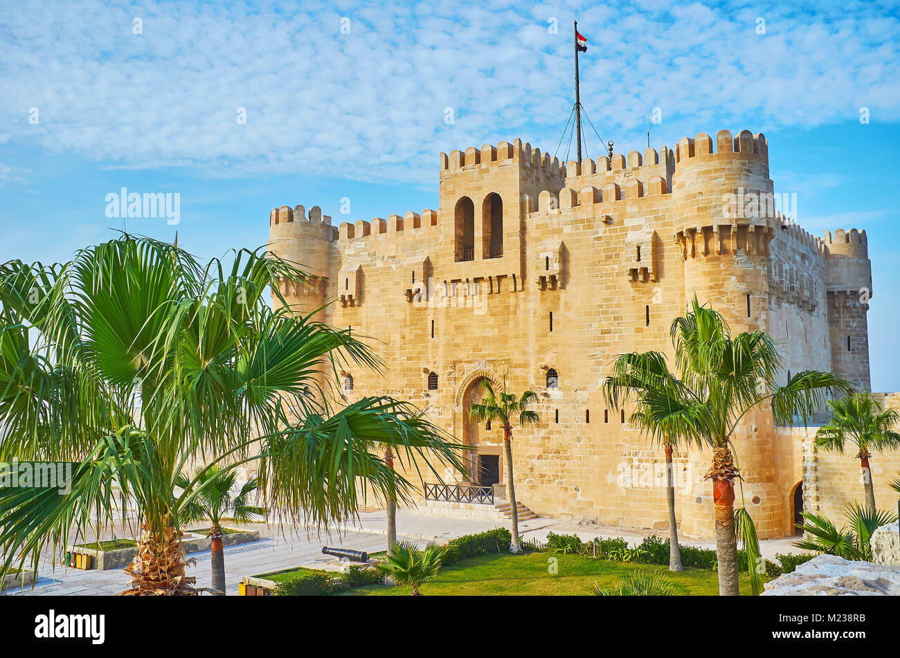 The old stone castle of Qaitbay is seen through the green palms ...