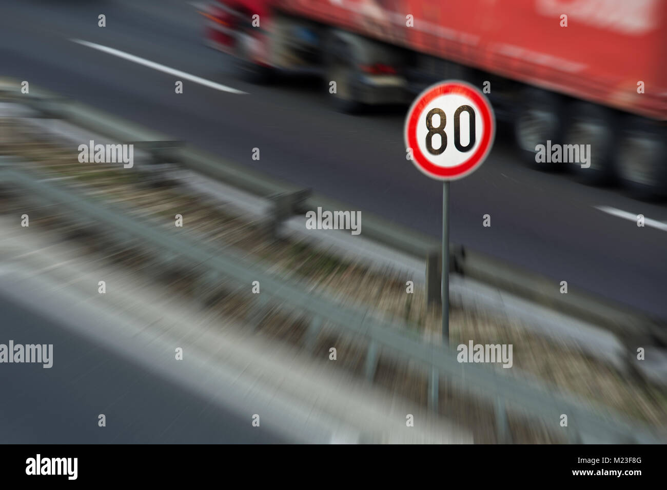 Defocused image of traffic sign showing 80 km/h speed limit on a highway with red truck driving ...