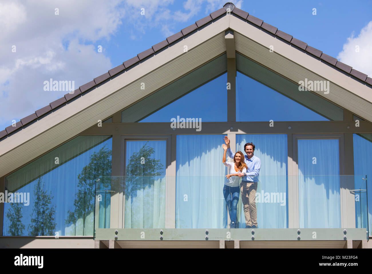 Happy couple standing on the balcony of their house and waving hands ...