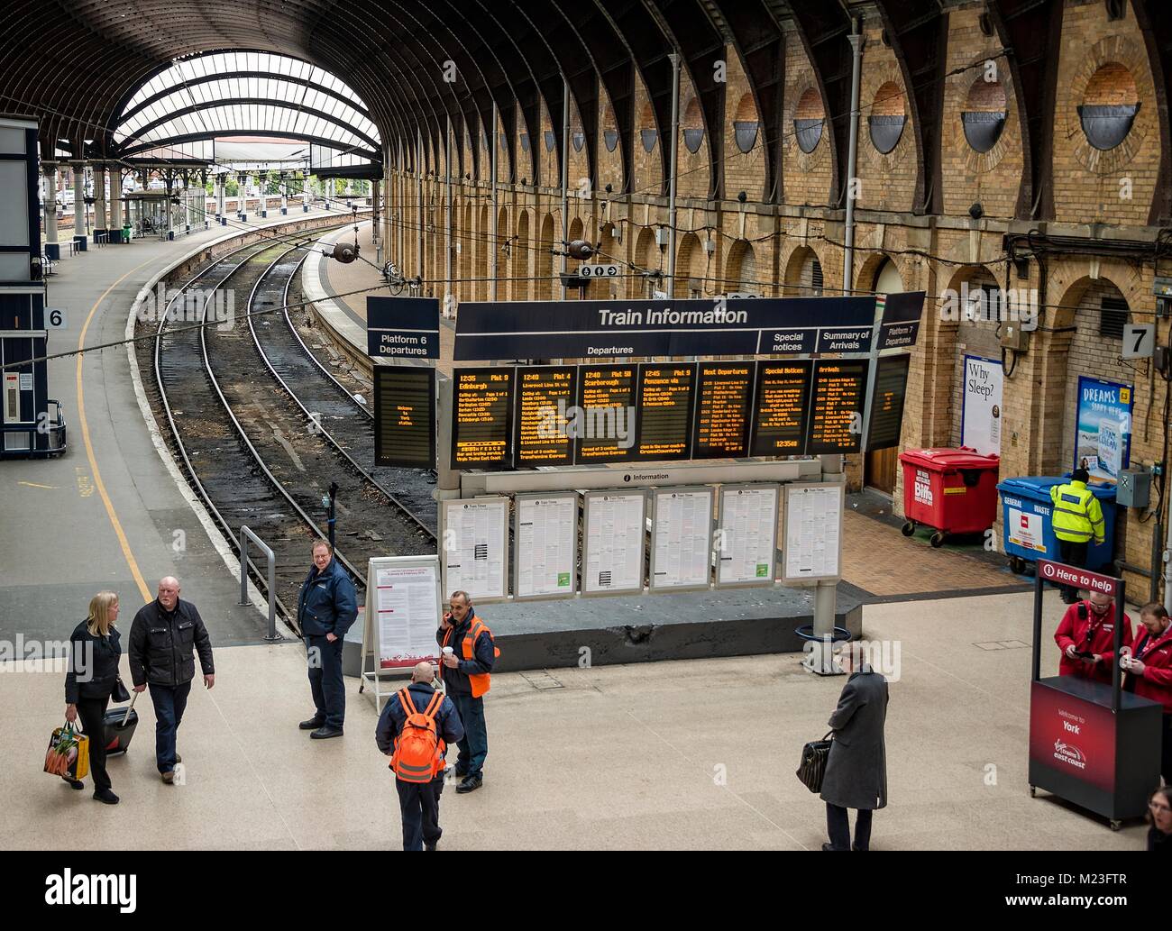 Passengers and railway crew underneath an electronic information board ...