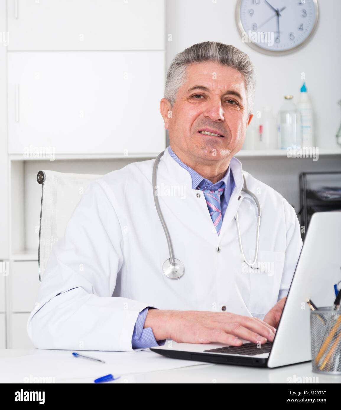 Doctor in white gown behind desk and computer at hospital office Stock ...