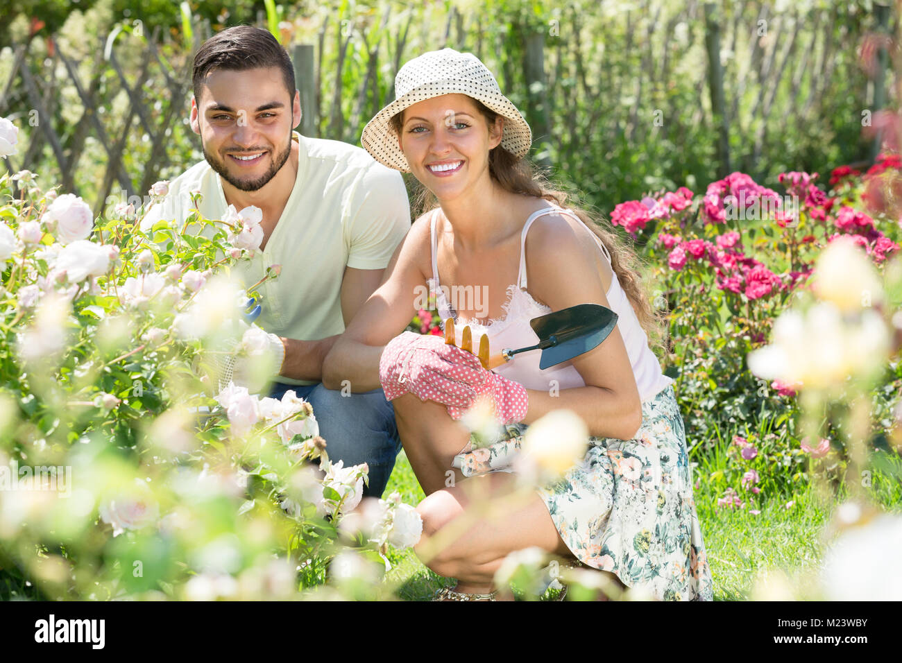 Smiling young couple with garden tools working together in garden at ...
