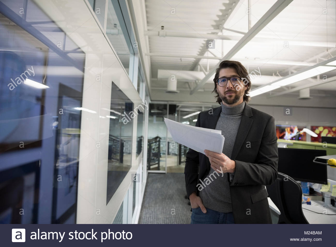 Portrait confident businessman with paperwork at screens in office ...