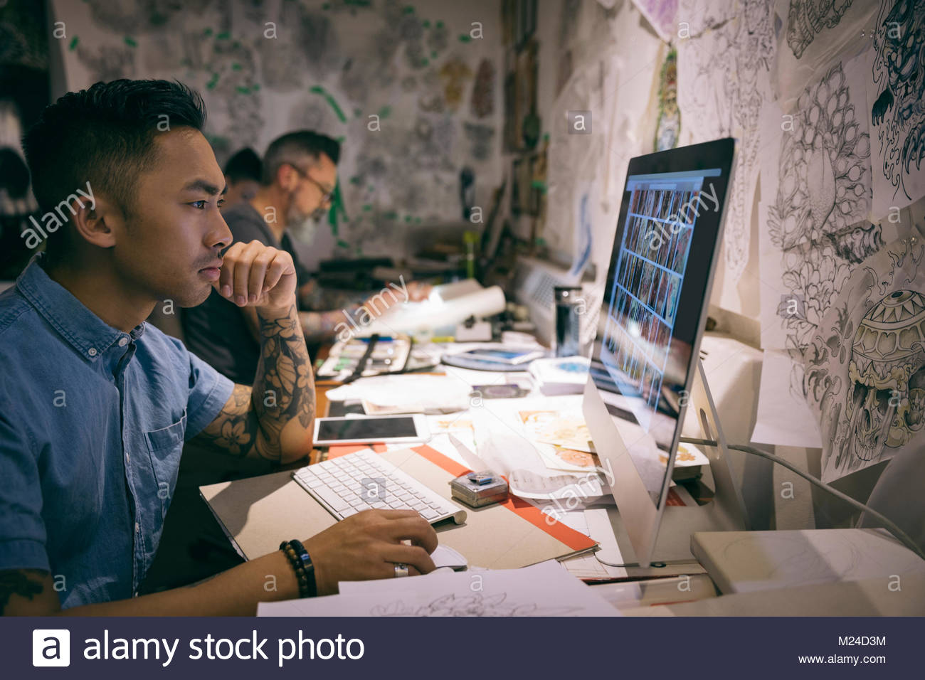 Tattoo artist viewing digital photographs on computer in tattoo studio ...