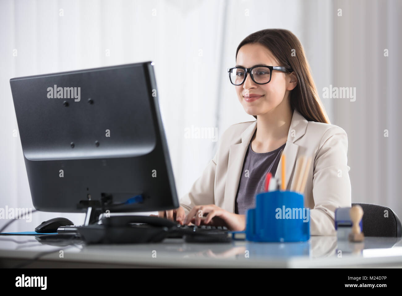 A Happy Young Businesswoman Wearing Eyeglasses Typing On Keyboard In ...