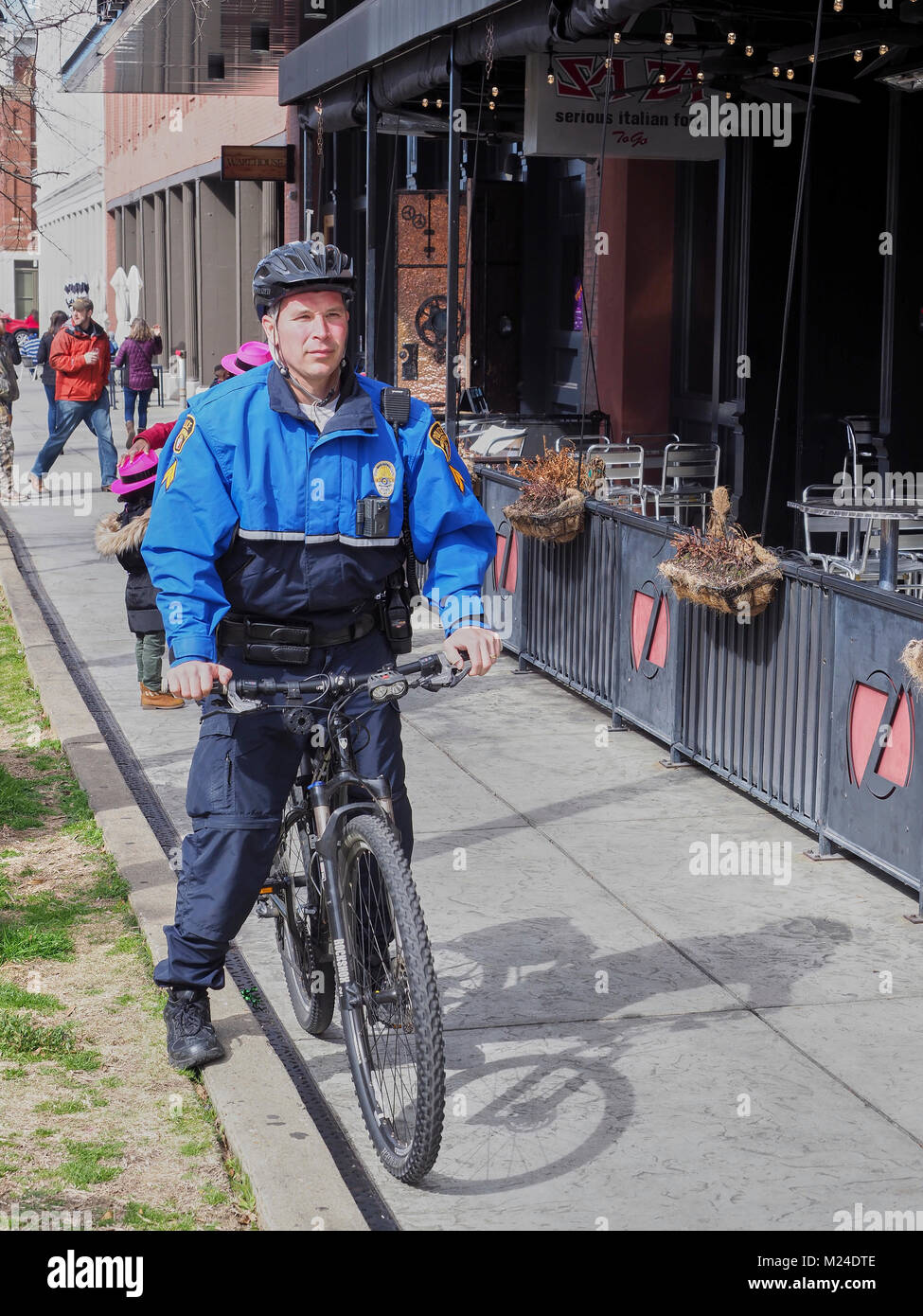 Police Officer on a bicycle conducts routine patrol on a city sidewalk ...