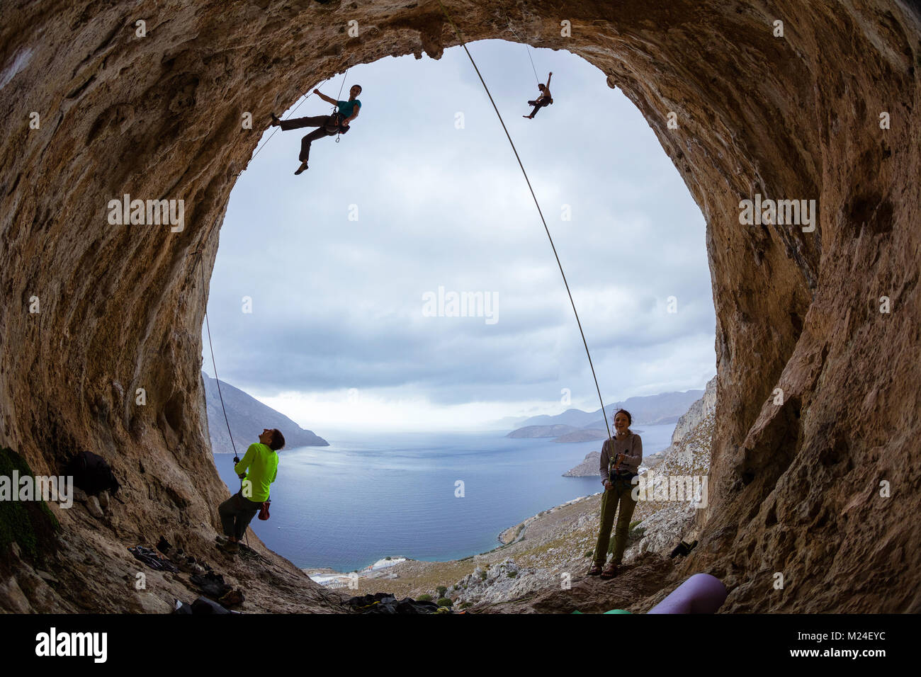 Rock climbers in cave: belayers watching leading climbers, two climbers ...
