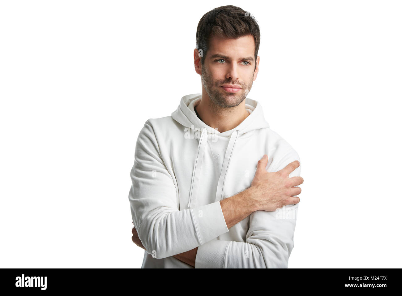 Portrait of young man wearing hoodie while standing at isolated white ...