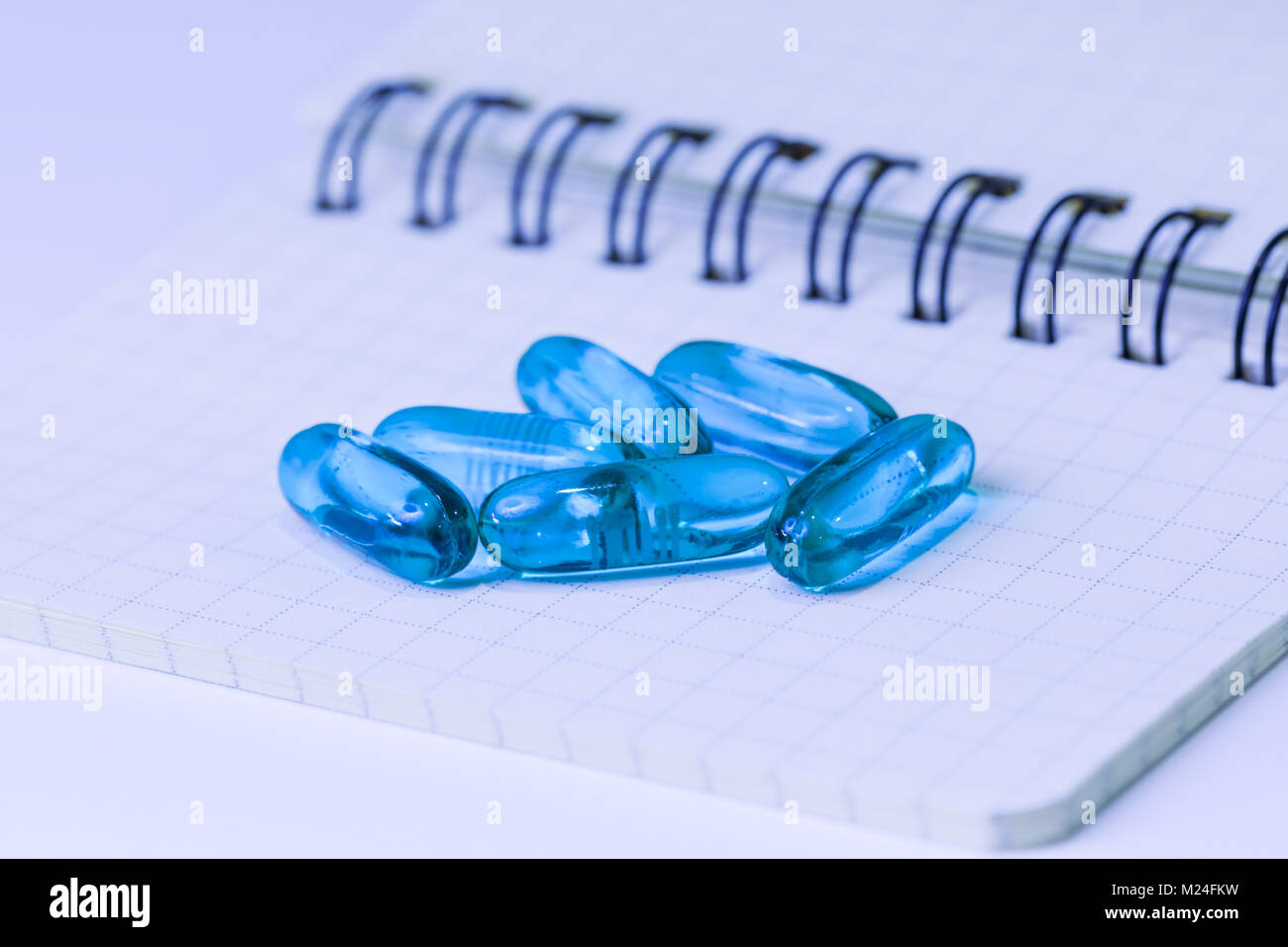 Pills on paper sheet. Blue pills in capsule shape scattered on a block ...