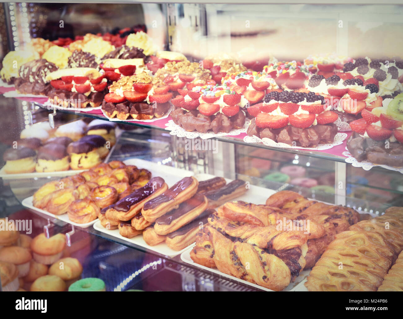 Sweet food behind a bakery shop window. Eclairs, baked goods and fruits ...