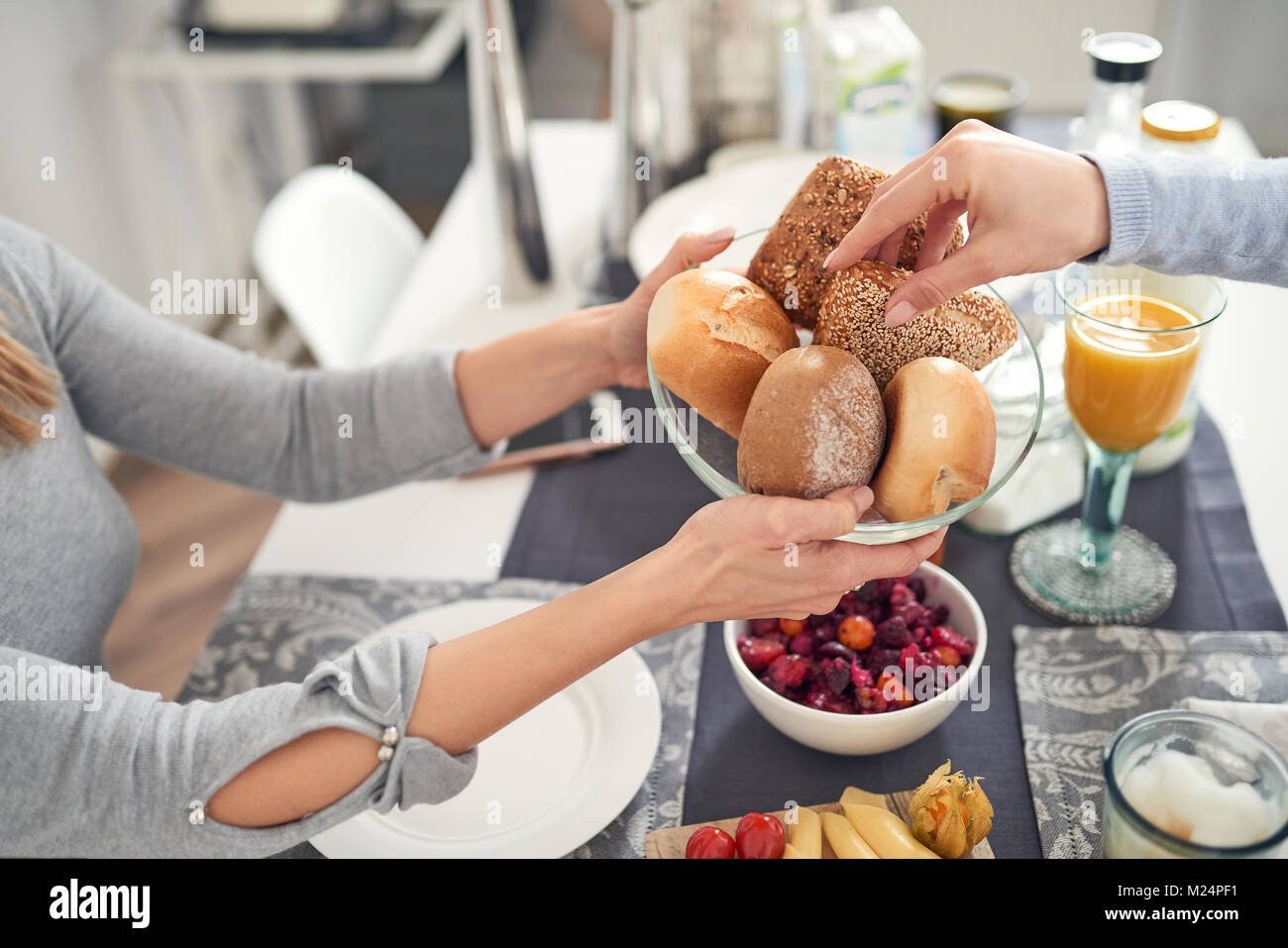 Two people eating breakfast selecting bread rolls of a plate from a ...