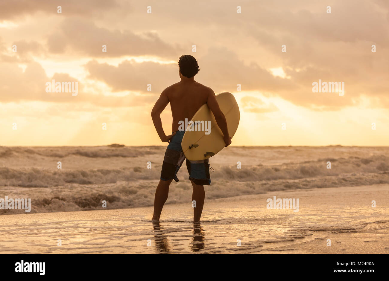 Rear view of young man male surfer with white surfboard looking at surf ...