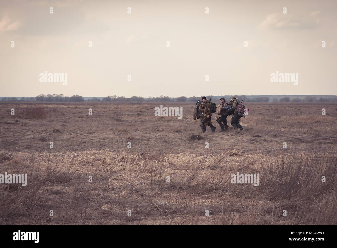 Group of men hunters gouing together through rural field in forward ...
