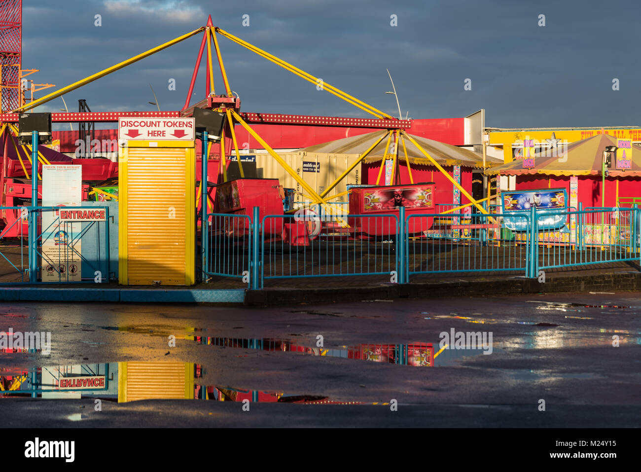 Deserted funfair rides in the sun with dark clouds and puddles Stock ...