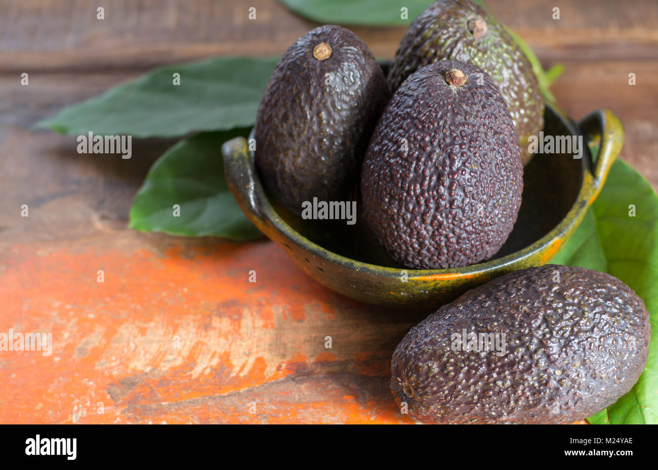 Raw ripe dark green whole avocados with leaves on wooden background ...