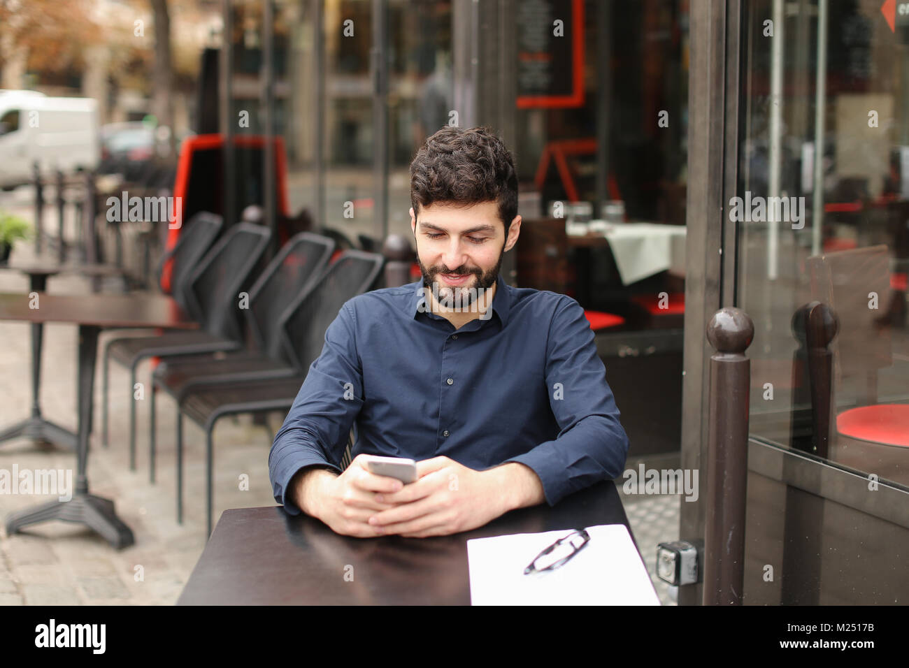 Happy man sitting at cafe table and chatting by smartphone with Stock ...