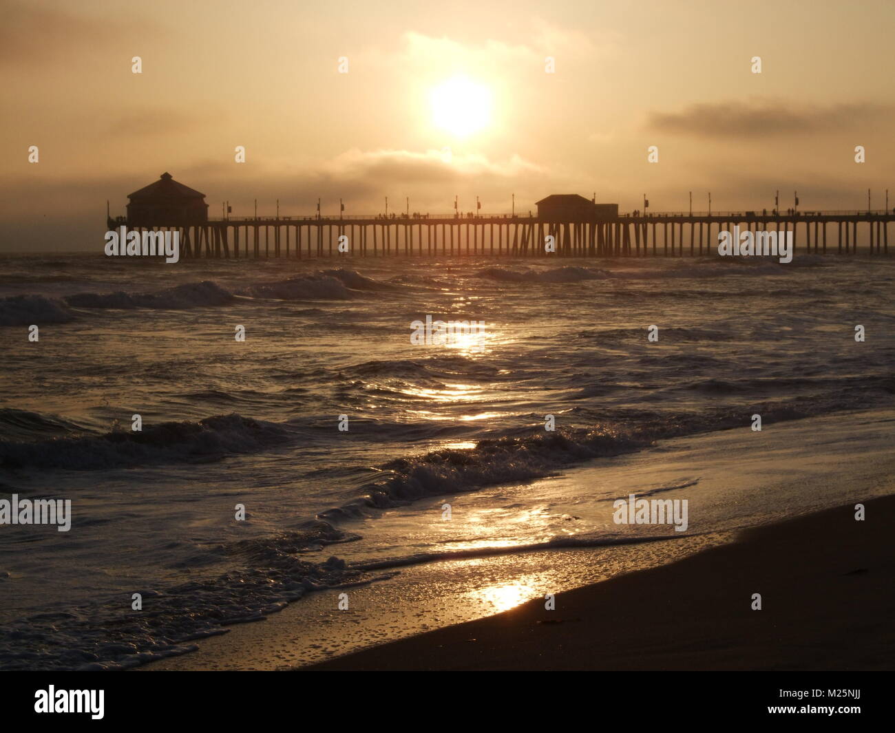 Sunset at Huntington Beach, ocean waves and lighthouse in the far back ...