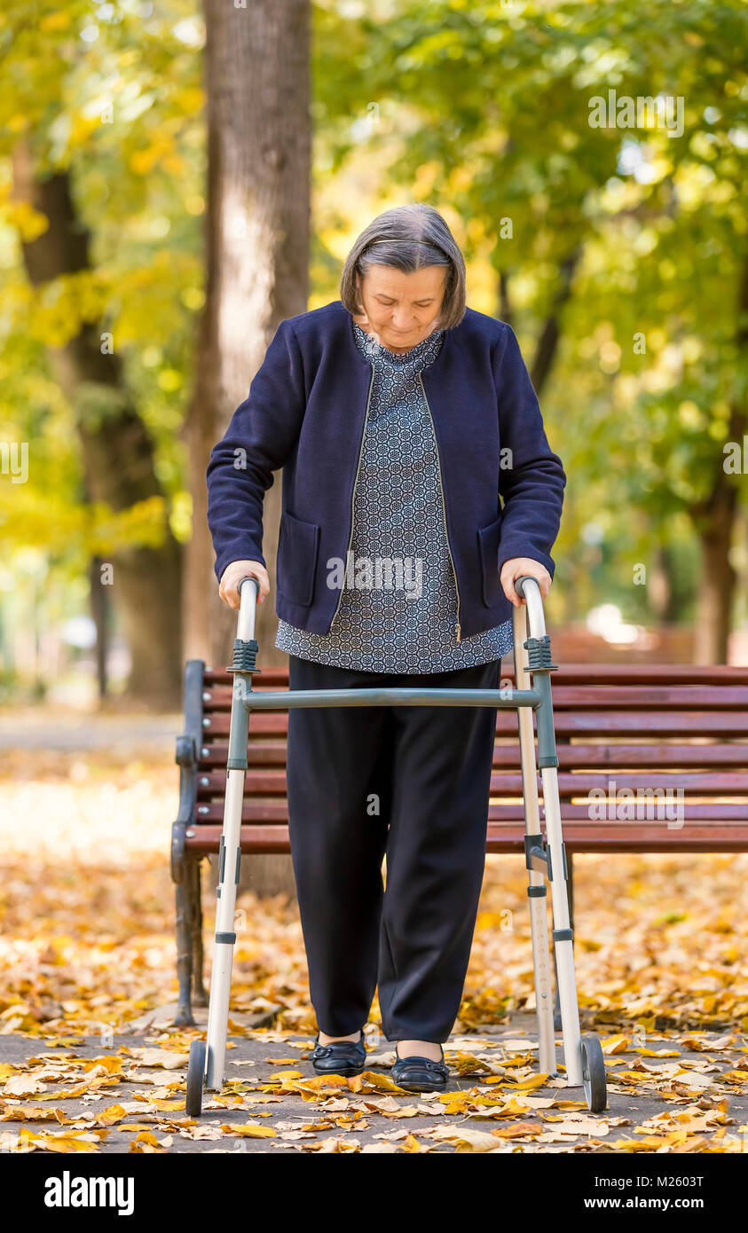 Senior woman with walker getting up from bench and walking outdoors in ...