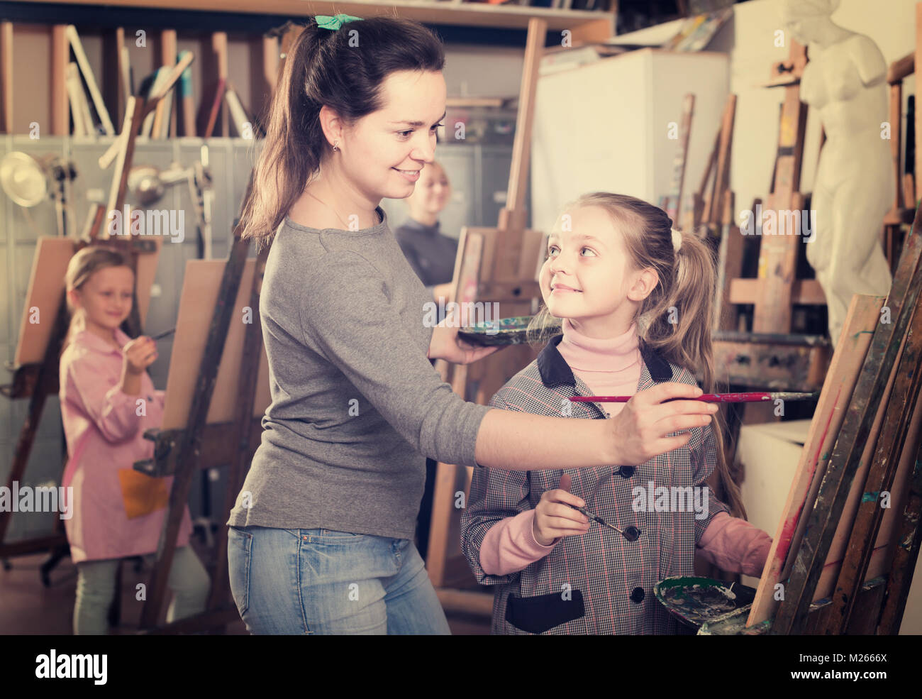 Smiling woman teacher assisting girl during drawing class at art studio ...
