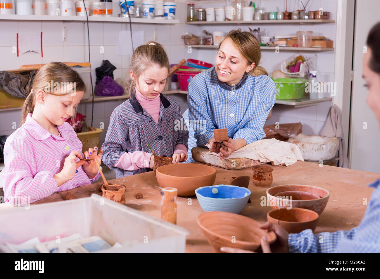 Smiling schoolgirls teacher shows how to make dishes from clay in class ...
