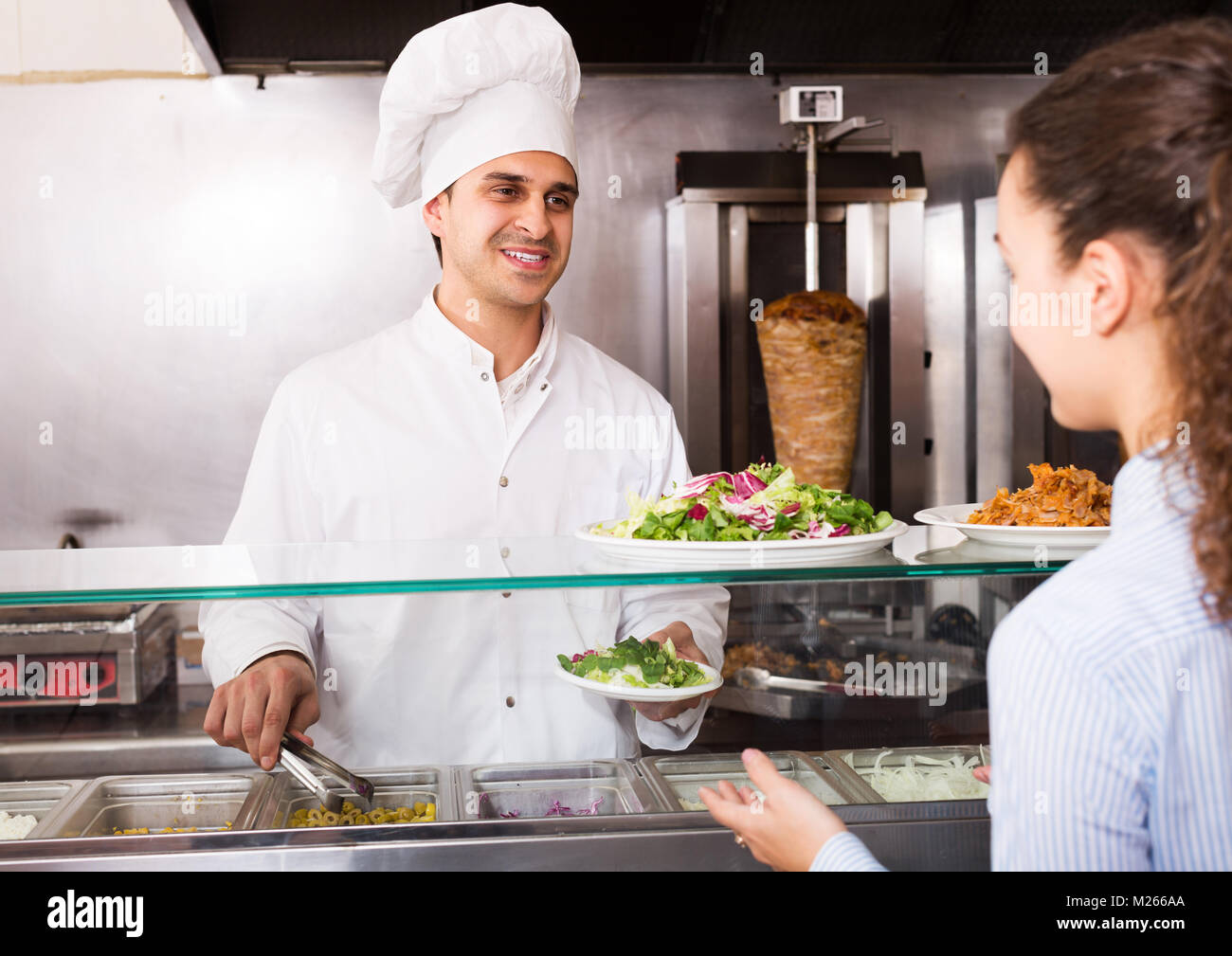 Positive adult male worker serving customer with smile at shawarma ...