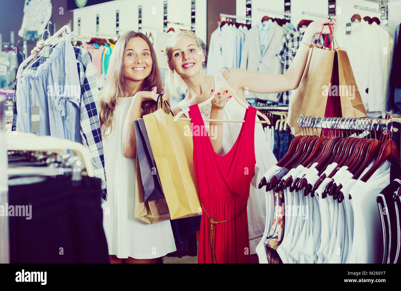 two joyful smiling girls holding clothes racks and shopping bags ...