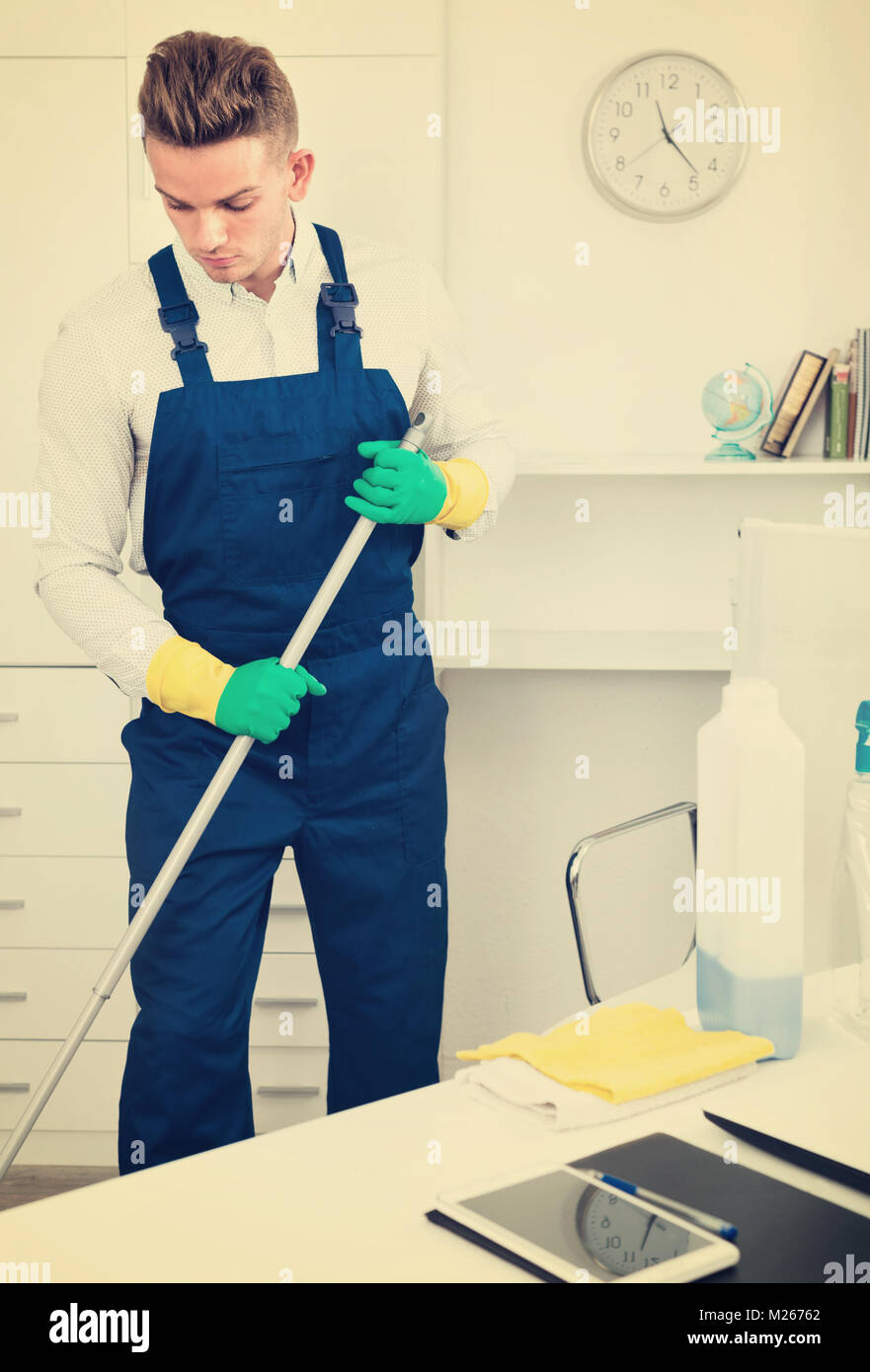 Friendly male professional janitor dusting in modern office interior ...
