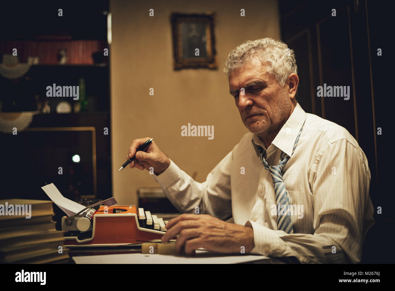 Retro senior man writer with pencil in his hand sitting at the desk and ...