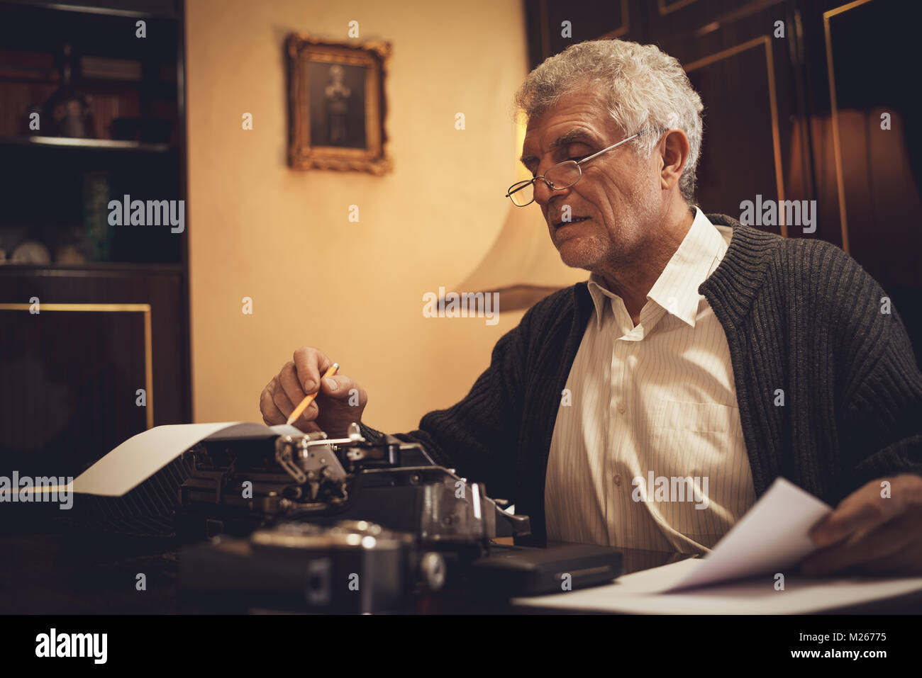 Retro senior man writer with glasses and pencil in his hand sitting at ...