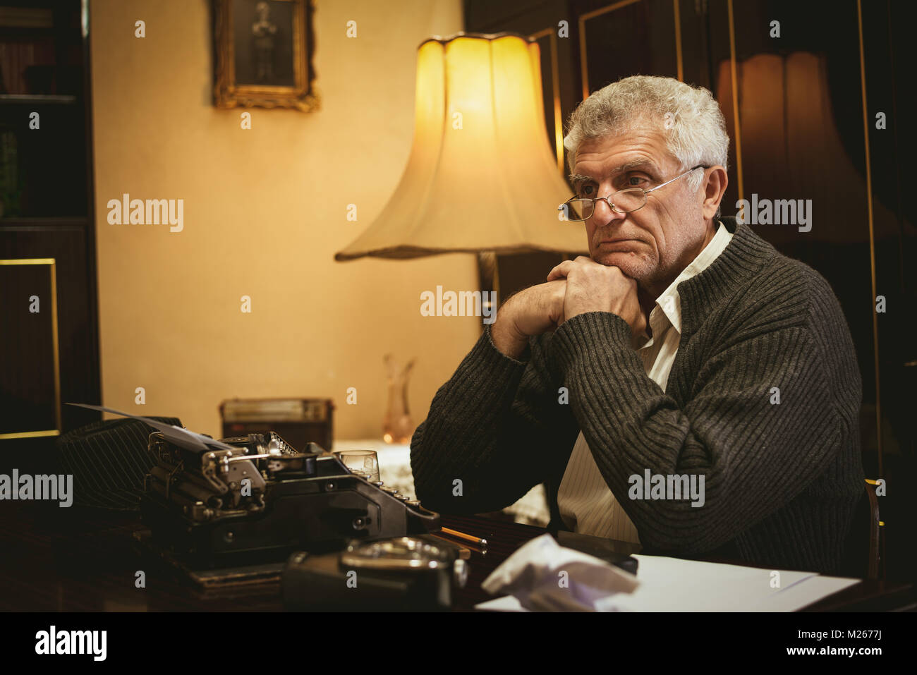 Pensive retro senior man writer with hat, sitting at the desk, looking ...