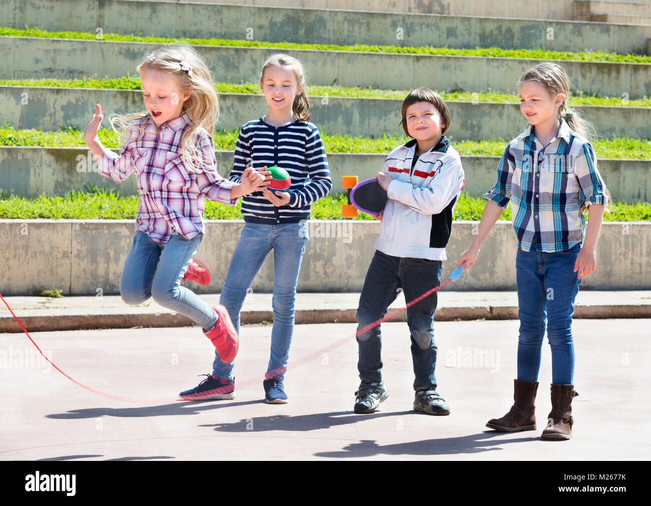 Happy children playing skipping rope jumping game and laughing outdoors ...