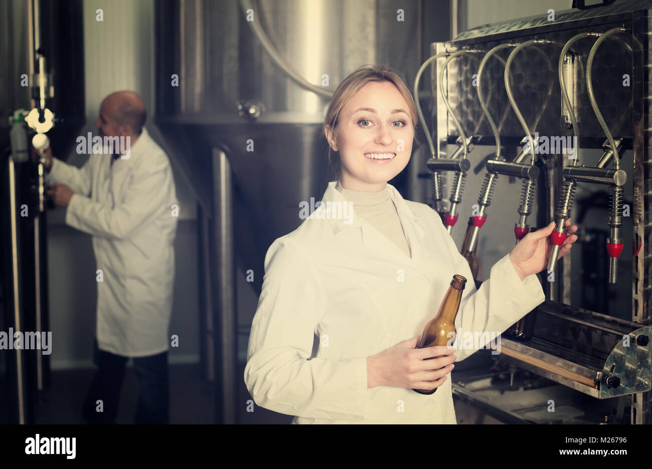 Smiling young woman employee bottling beer in glass bottles on modern ...