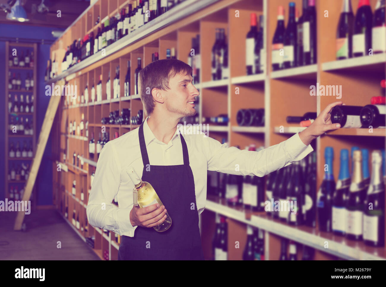 Portrait young man seller wearing uniform having bottle of wine in wine ...
