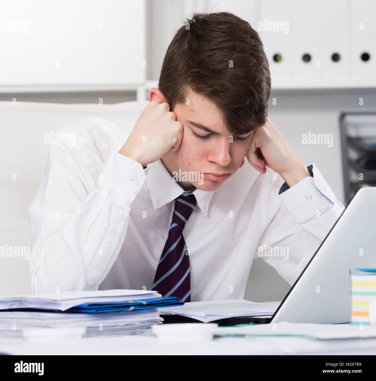 Boring teenager reading documents near the laptop in the office Stock ...