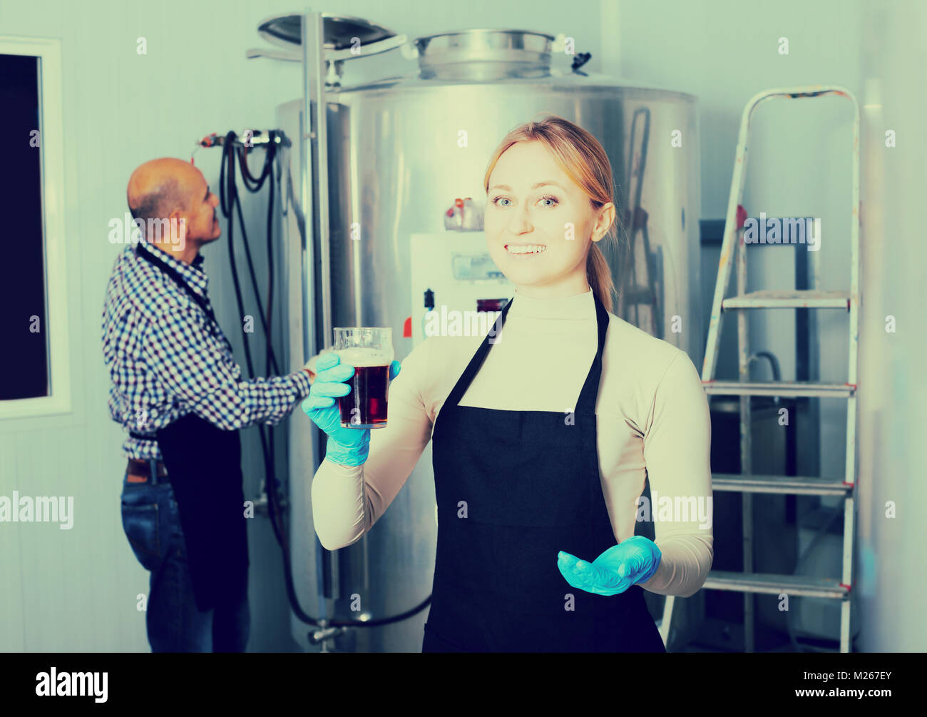 Portrait of positive woman employee in modern beer production facility ...