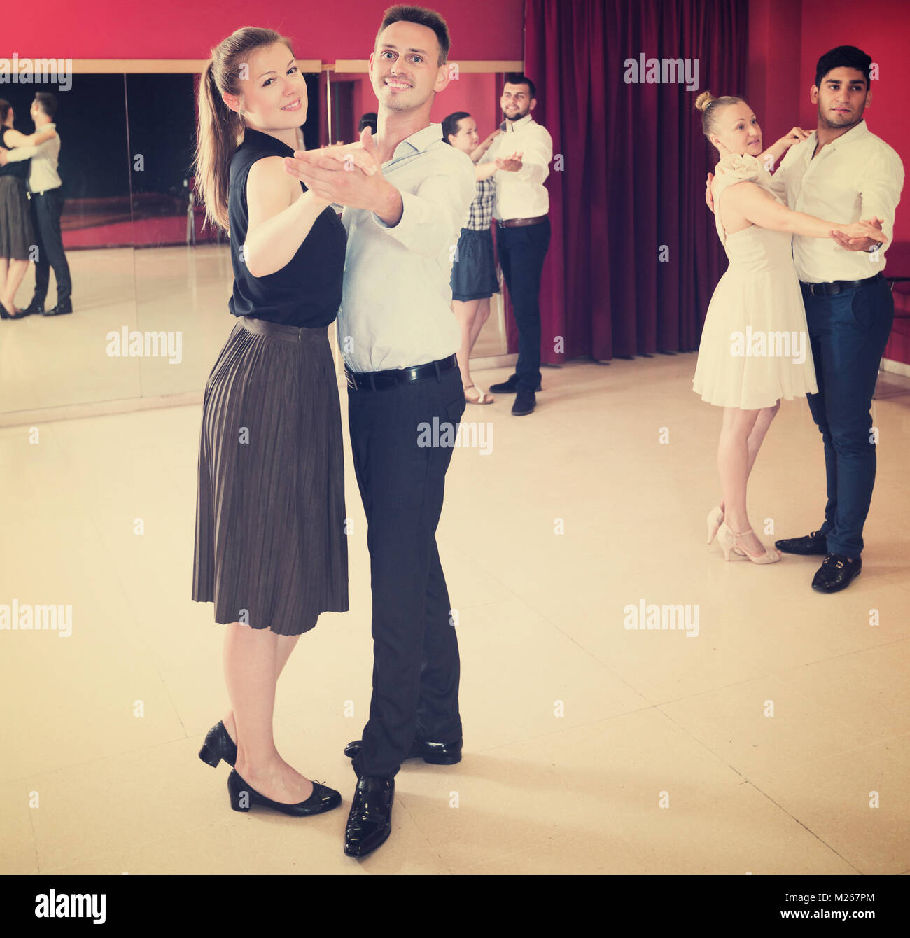 Positive young people dancing together slow ballroom dances in pairs ...