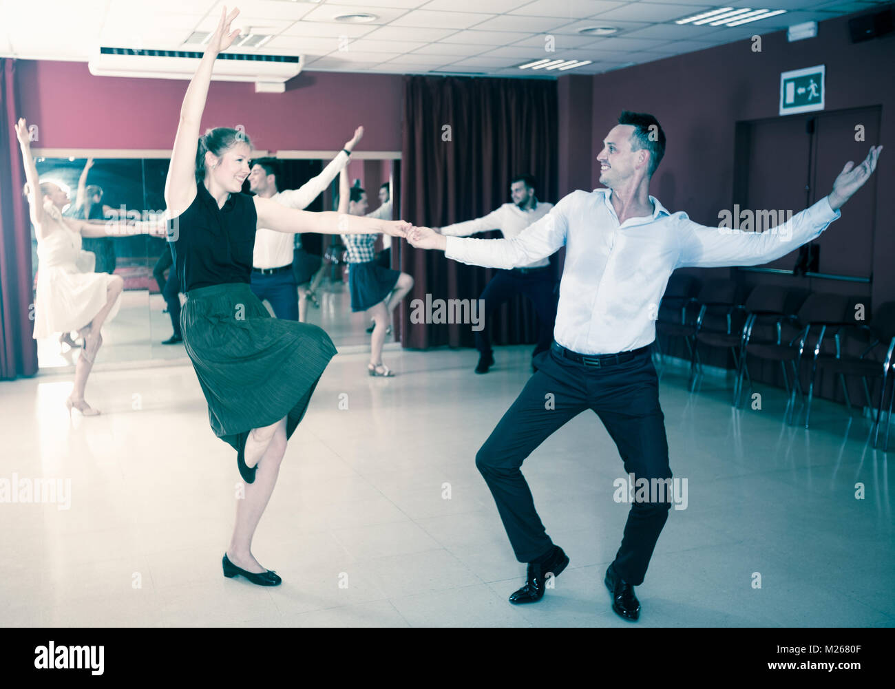 Young smiling people practicing vigorous jive movements in dance class ...