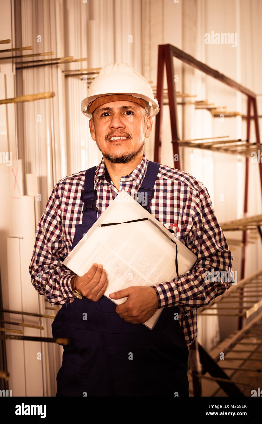 Middle age workman in helmet with documents at workshop Stock Photo - Alamy